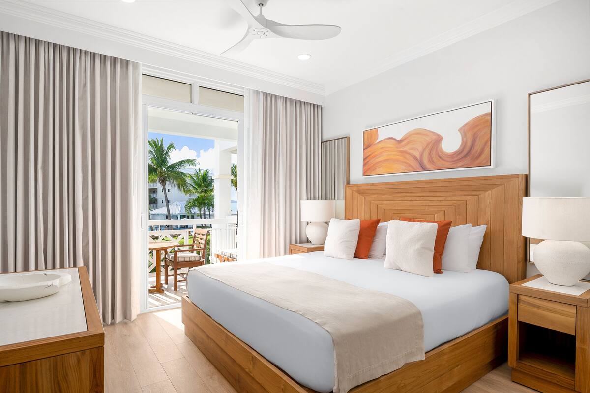 Quarto de hotel com cama, mesas de cabeceira, ventoinha no teto, vista para o exterior e um quadro na parede.
