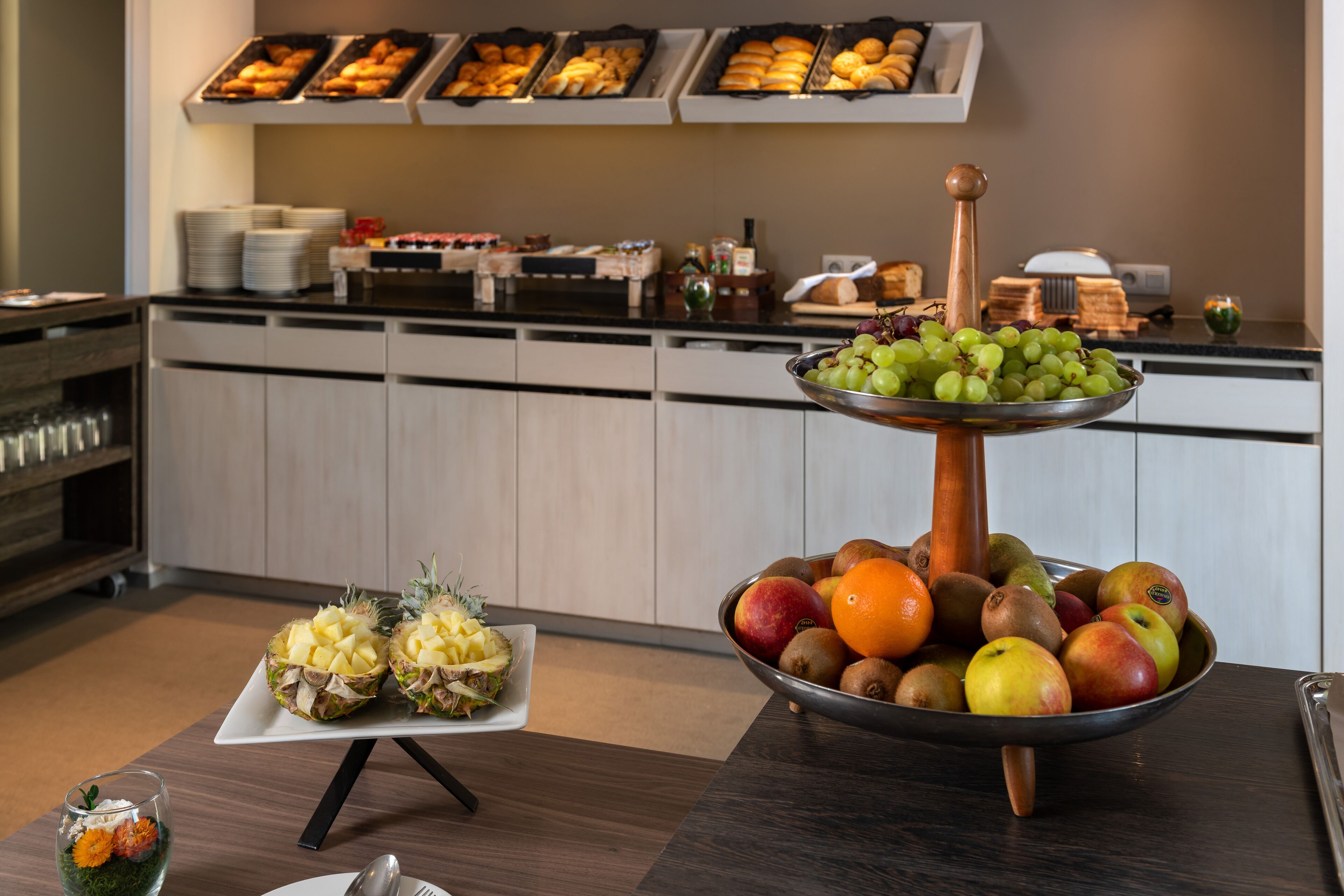 Buffet com diversos alimentos, uma saladeira de frutas e um copo de água sobre uma mesa.