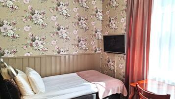 Quarto com cama, escrivaninha, cadeira, televisão e papel de parede floral.