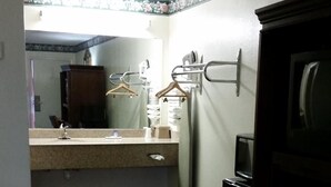 Quarto de hotel com duas camas, banheiro com espelho, pia e televisão.
