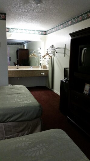 Quarto de hotel com duas camas, banheiro com espelho, pia e televisão.