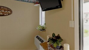 Quarto com televisão de tela plana montada, ar condicionado fixado parede e janela com vista para prédios.
