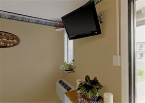 Quarto com televisão de tela plana montada, ar condicionado fixado parede e janela com vista para prédios.