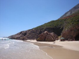 Uma praia com falésias rochosas, céu claro e algumas pessoas.