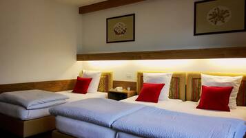 Quarto de hotel com duas camas, cada uma com cabeceira, roupa de cama branca e almofadas vermelhas. Quadros emoldurados na parede acima das camas.