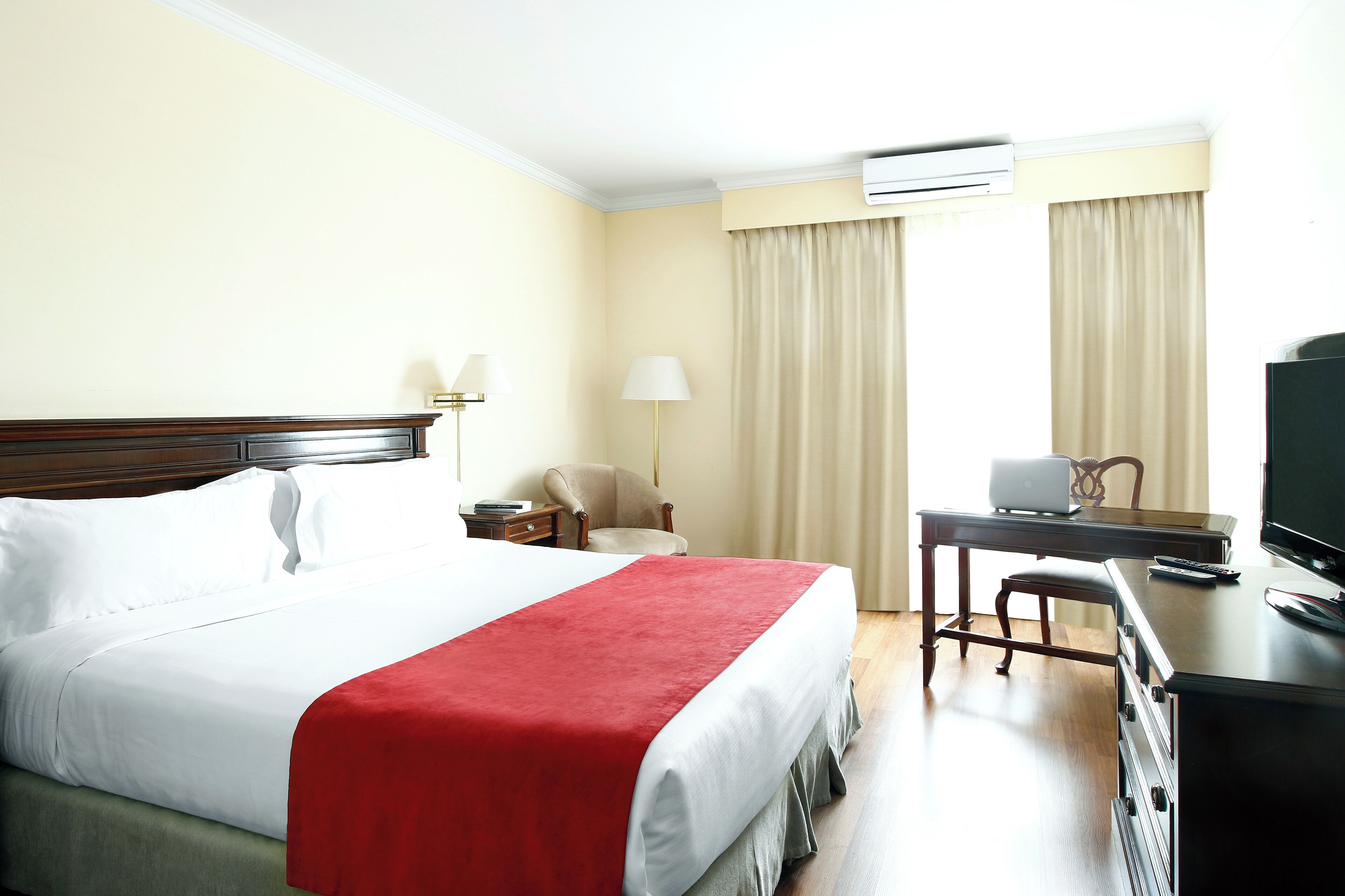 Quarto de hotel com cama, escrivaninha, cadeira, televisão e ar condicionado.
