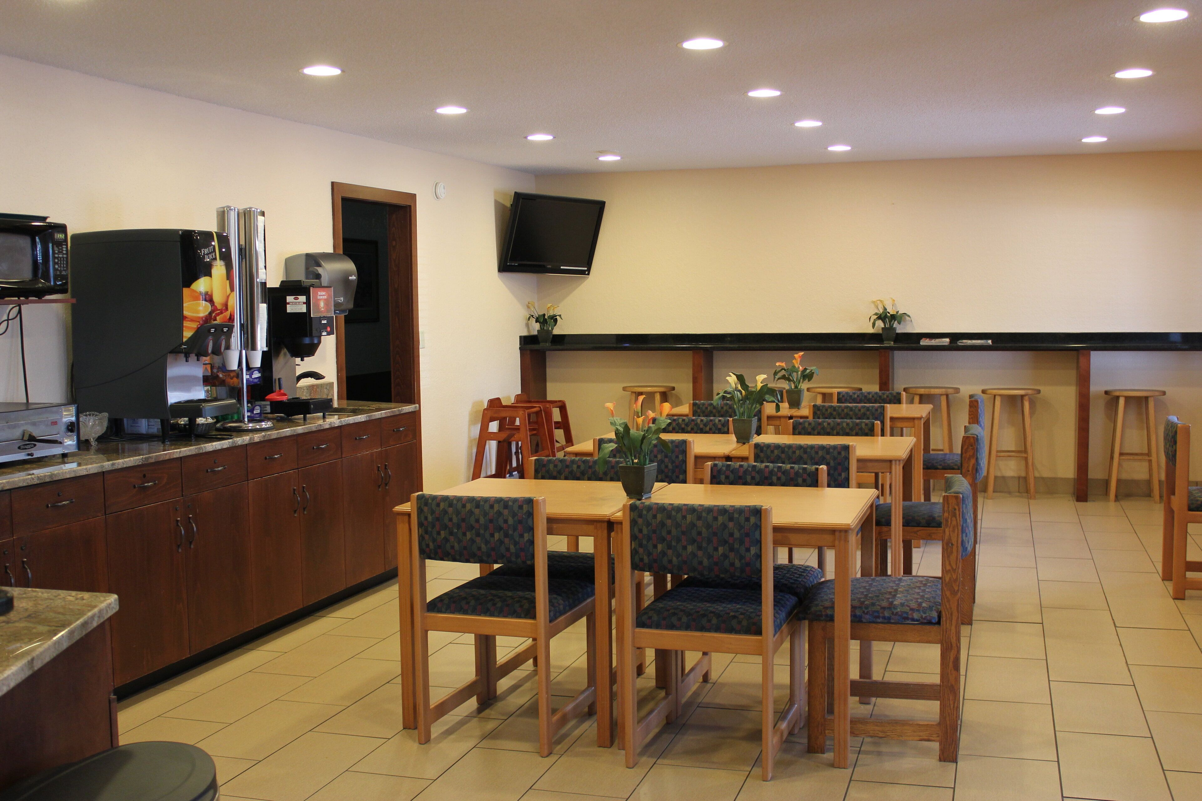 Um restaurante com mesas e cadeiras de madeira, uma máquina de café e uma TV fixada na parede.