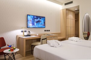 Quarto de hotel com cama, escrivaninha, cadeira, televisão e guarda-roupa.