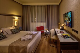 Quarto de hotel com duas camas, uma escrivaninha, uma cadeira, televisão e janela com cortinas.