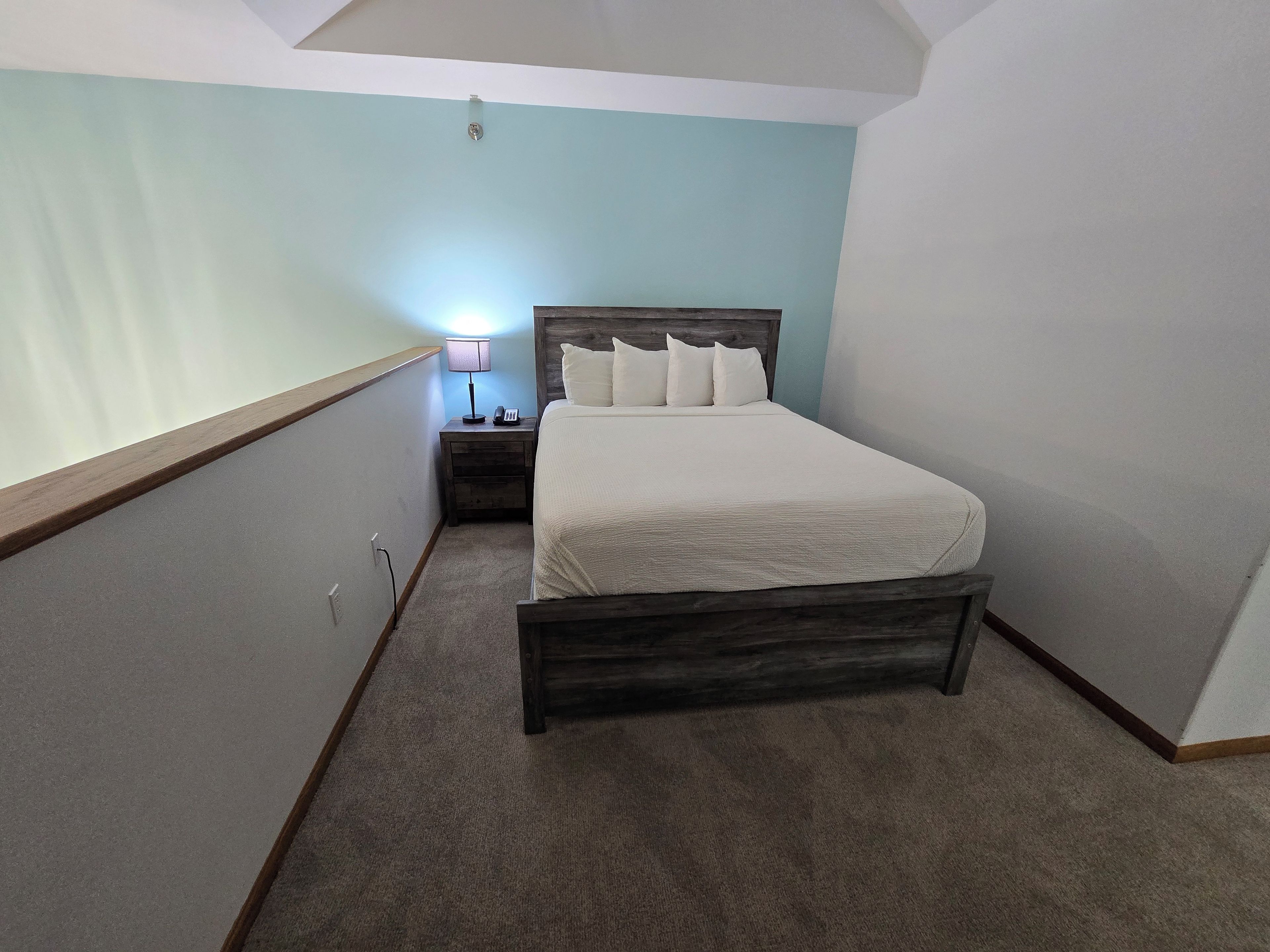 Quarto com cama, mesa de cabeceira, abajur e luz no teto.