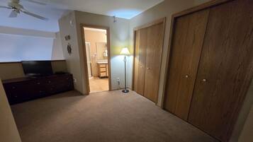 Quarto com ventilador de teto, televisão sobre uma cômoda, abajur e armário.
