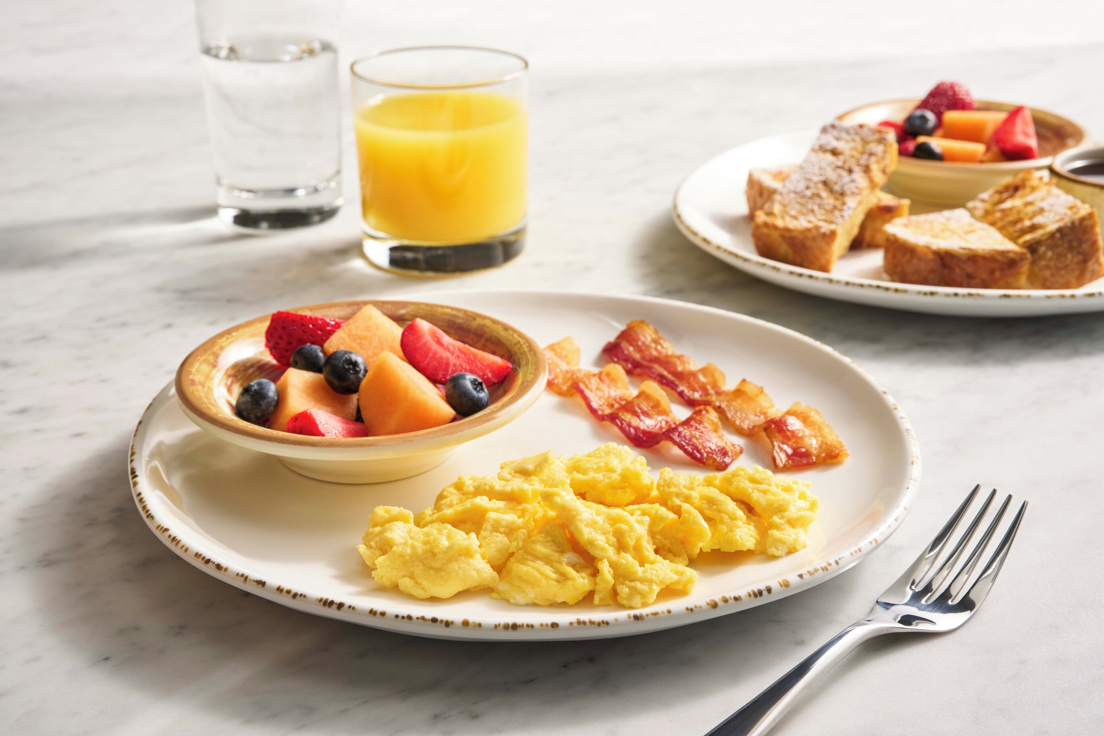 Prato de café da manhã com ovos mexidos, bacon e frutas, incluindo morangos e mirtilos.