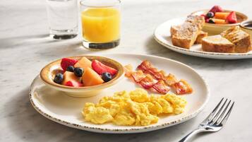 Prato de café da manhã com ovos mexidos, bacon e frutas, incluindo morangos e mirtilos.