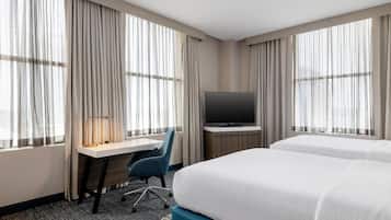 Quarto de hotel com cama, escrivaninha, cadeira, televisão e cortinas.