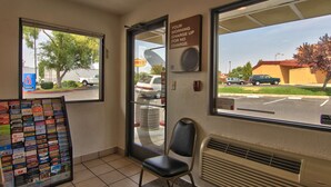 Um saguão de hotel com uma cadeira, uma janela com vista para o estacionamento e um aviso sobre serviço de recarga matinal.