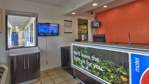 Balcão de recepção de motel com tela digital exibindo uma mensagem, uma televisão e um espelho.