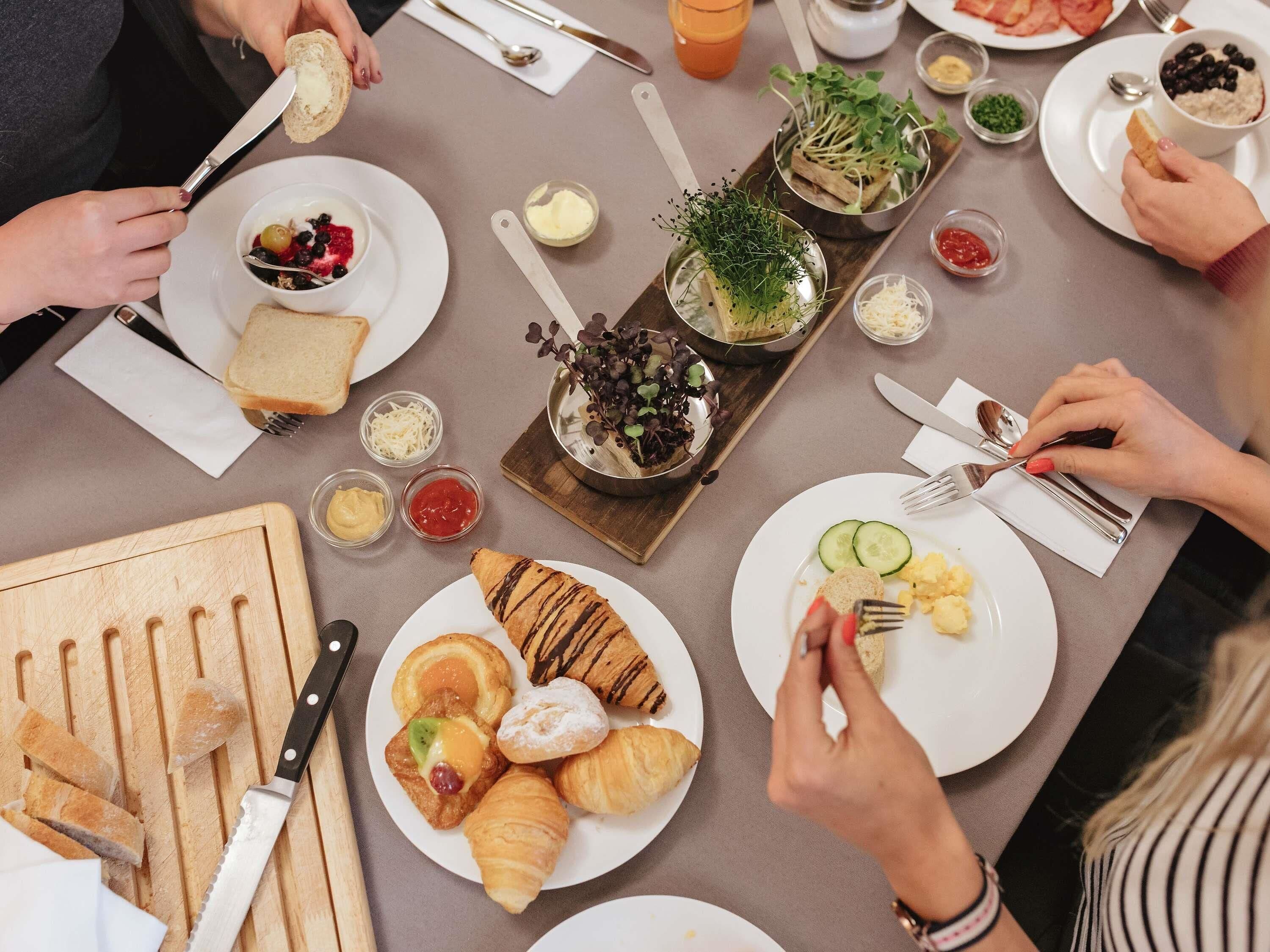 Um grupo de pessoas jantando à mesa, com diversos pratos, incluindo pão, croissants e uma salada.