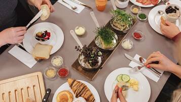 Um grupo de pessoas jantando à mesa, com diversos pratos, incluindo pão, croissants e uma salada.