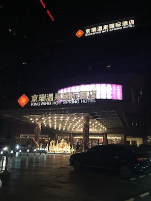 Exterior do Hotel King Wing Hot Spring, com letreiros iluminados e área de entrada coberta.