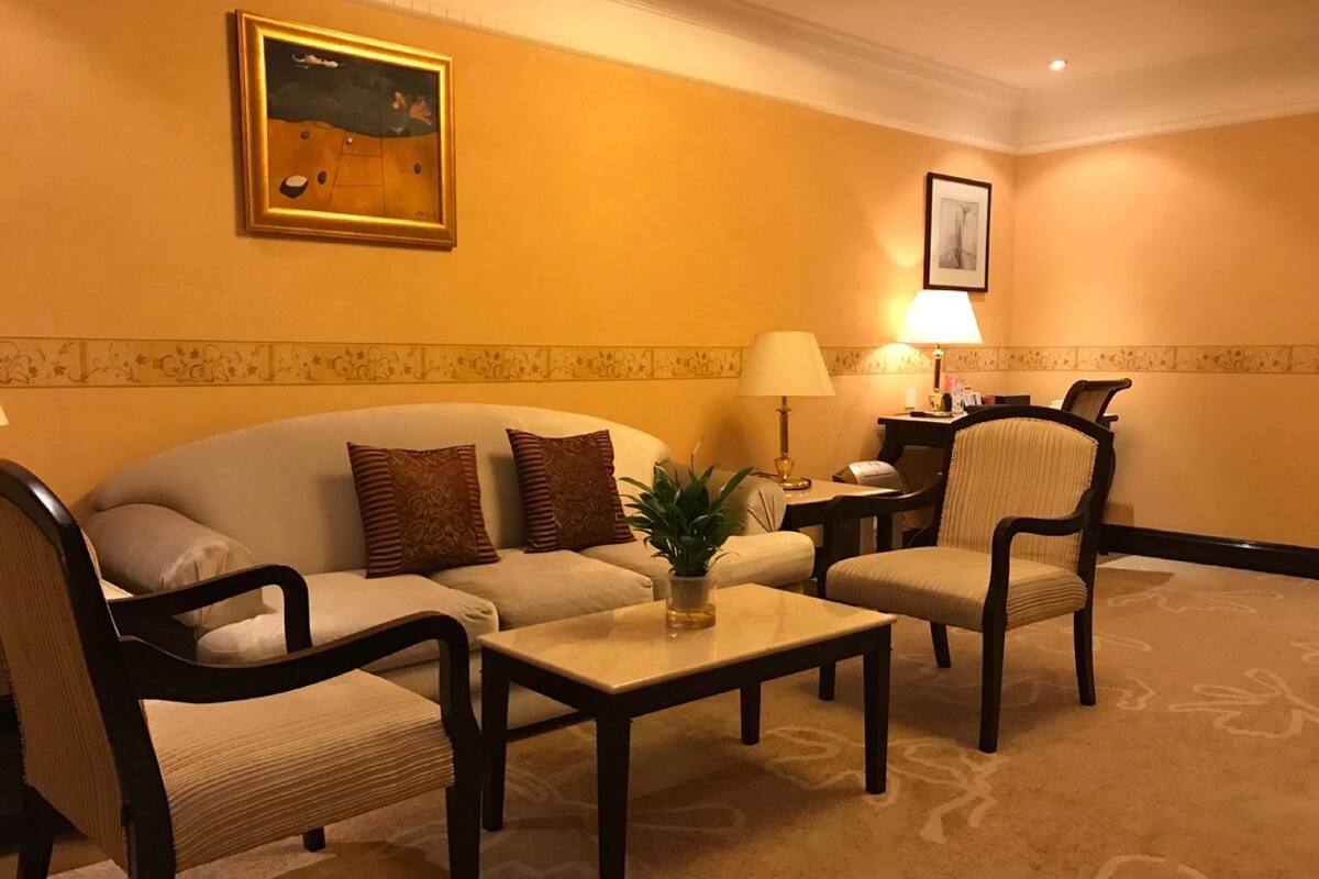 Quarto de hotel com sofá, duas poltronas, mesa de centro, abajur e um quadro na parede.