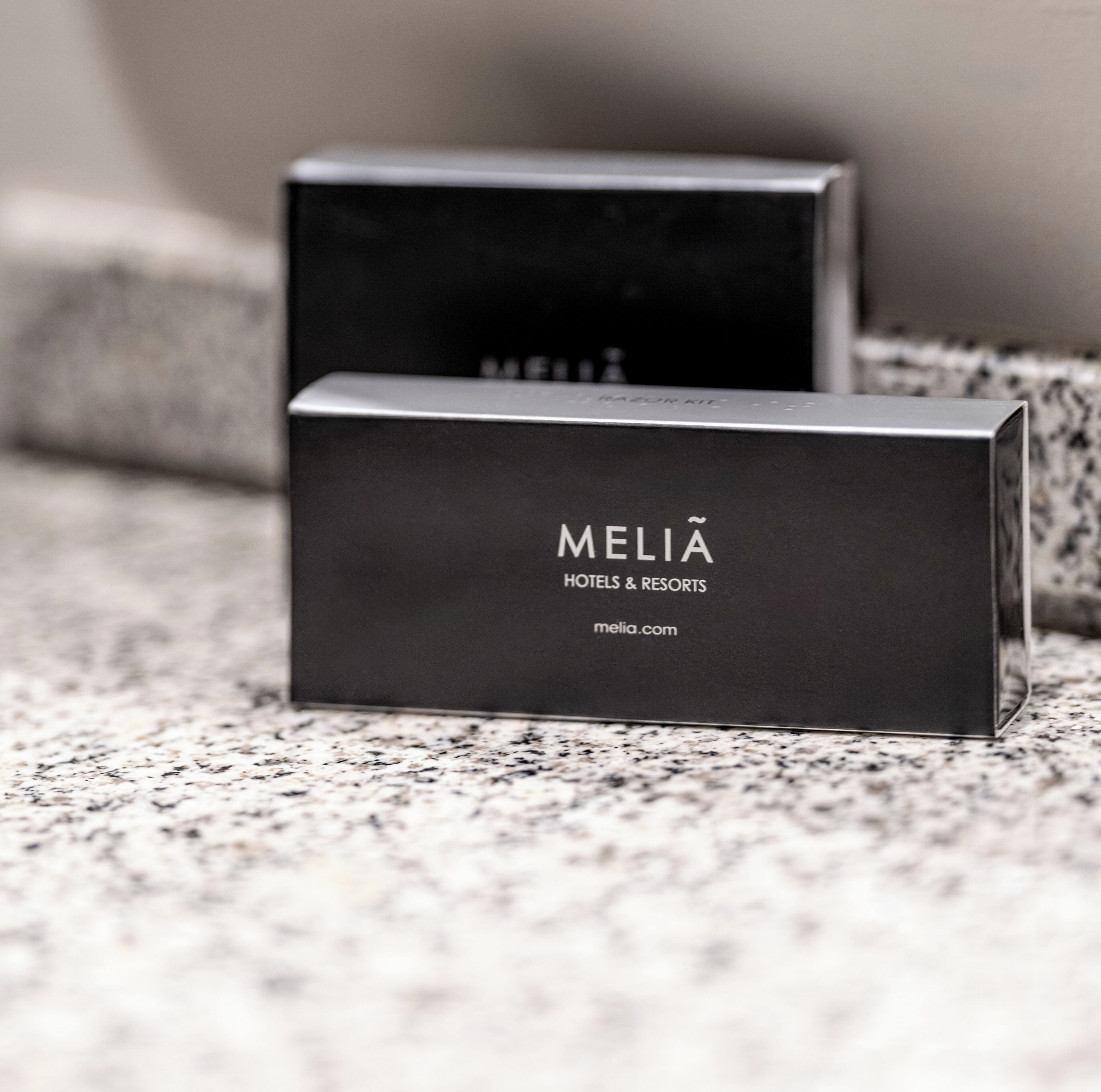Duas caixas pretas com a inscrição 'MELIA HOTELS & RESORTS' e 'melia.com' sobre uma superfície texturizada.