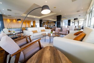Um hall de hotel moderno com uma área de estar ampla, incluindo sofás e poltronas, e uma mesa de centro grande.