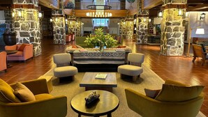 Um hall espaçoso com pilares de pedra, uma área de estar central com sofás e uma mesa de centro, e luminárias pendentes.