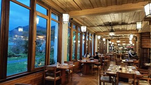 Um restaurante espaçoso com interiores em madeira e grandes janelas que oferecem vistas panorâmicas.