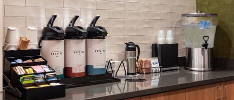 Uma estação de café com vários dispensadores de café, um dispensador de água e uma seleção de cápsulas de café e lanches.
