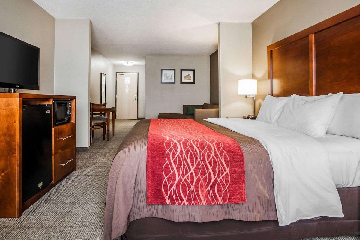 Quarto de hotel com cama, televisão, secretária e cadeira.