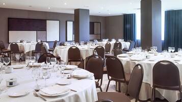 Sala de conferências com várias mesas preparadas para refeições, equipada com cadeiras e utensílios de jantar.