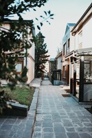 Um caminho pavimentado estreito, ladeado por edifícios com grandes janelas e portas, que leva a um ponto central.