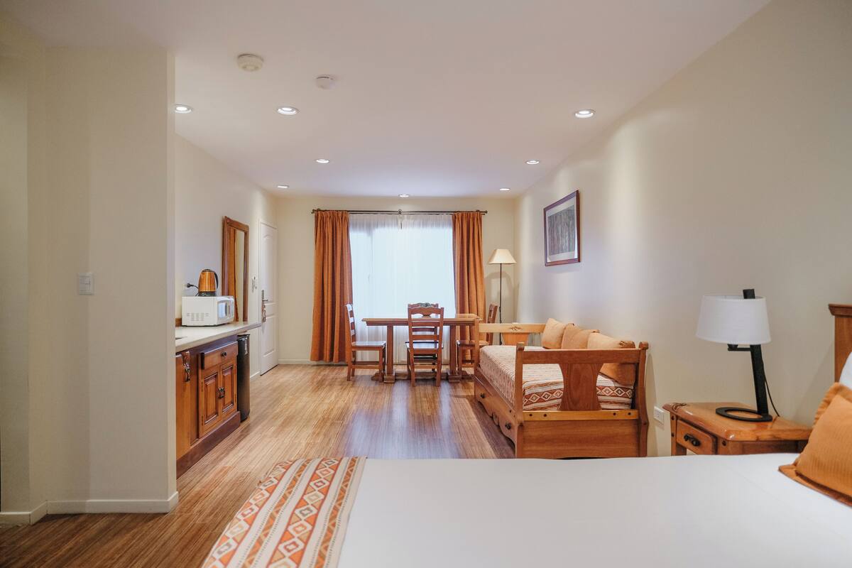 Quarto de hotel com cama, escrivaninha, cadeira, mesa e micro-ondas.