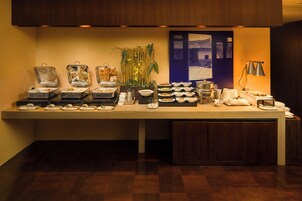 Disposição de buffet com diversos recipientes de comida e uma planta decorativa.
