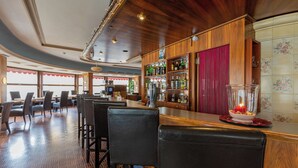 Uma área de bar com painéis de madeira, banquetas e uma vitrine de vidro com garrafas.