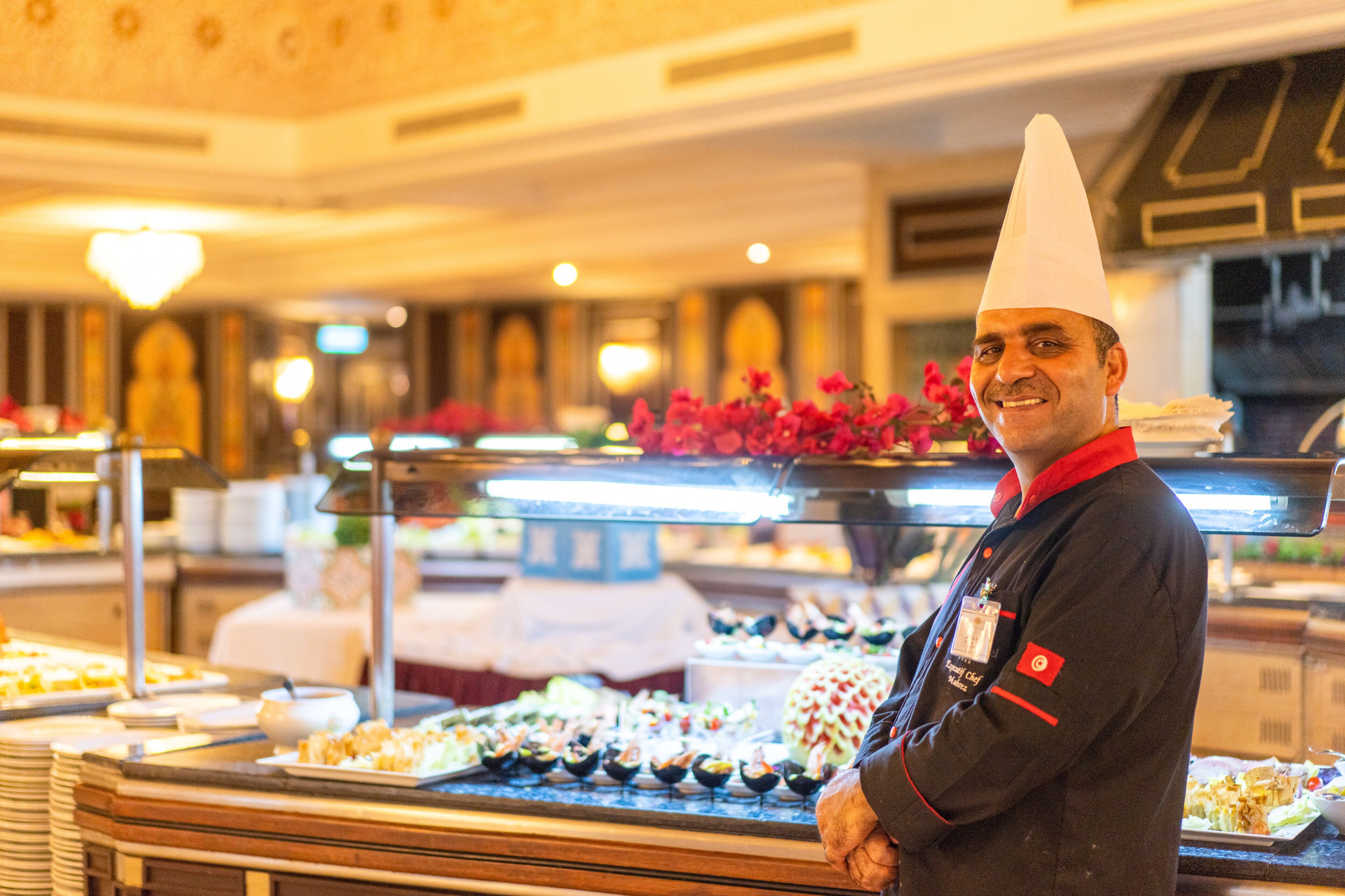 Uma área de buffet com diversos alimentos e um atendente de buffet uniformizado.