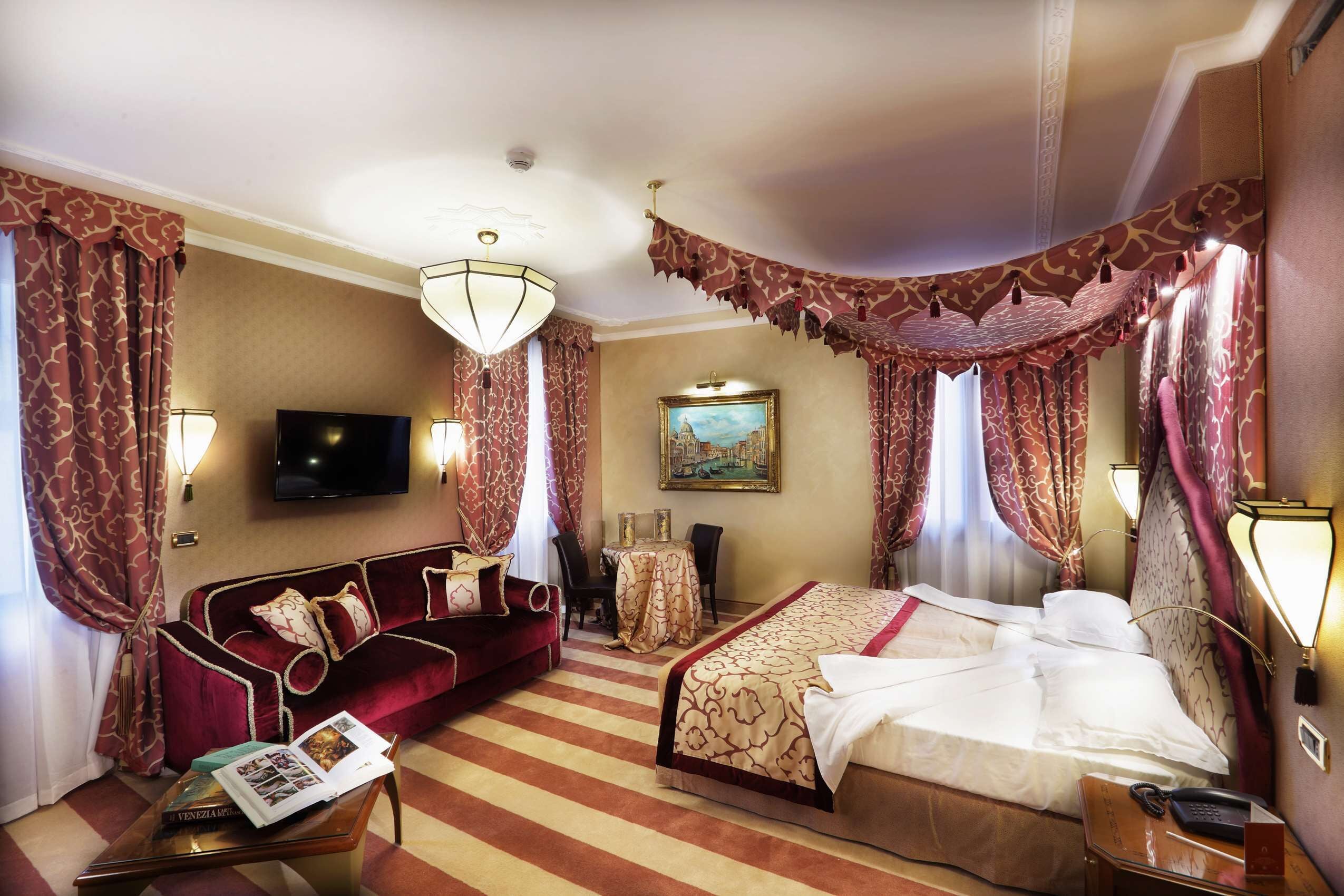 Quarto de hotel com uma cama grande, um sofá, uma televisão e uma mesa com um quadro.