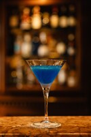 Um copo de martini com líquido azul sobre uma superfície de mármore.