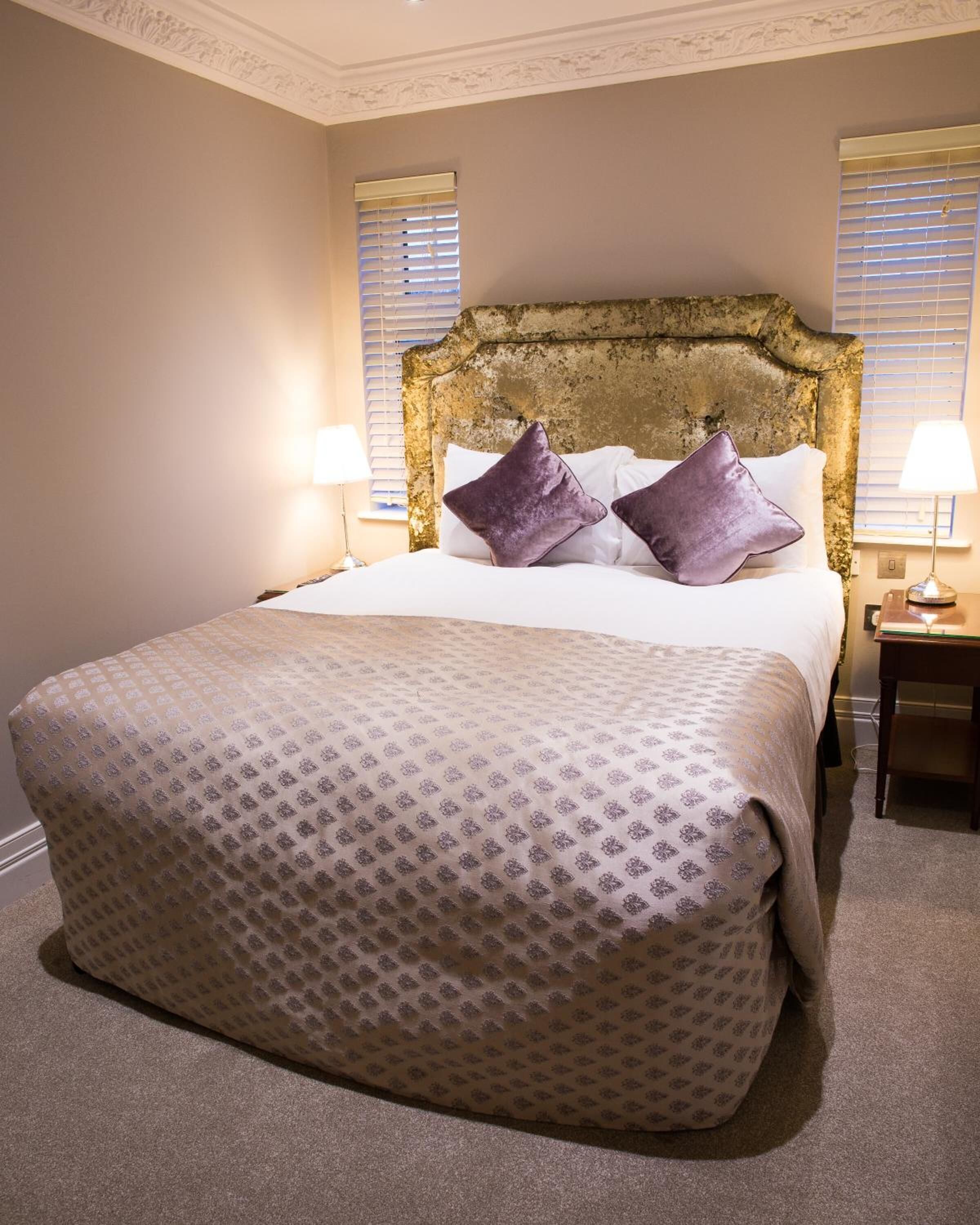 Quarto de hotel com uma cama grande, duas mesas de cabeceira e uma cabeceira com design texturizado.