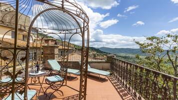 Um terraço com um gazebo de ferro forjado, cadeiras de descanso e uma mesa com uma garrafa e um copo.