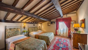 Quarto com duas camas, vigas de madeira no teto, cortina vermelha e uma pequena mesa com abajur.