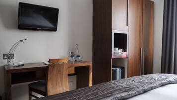 Quarto de hotel com cama, escrivaninha com cadeira, televisão fixada na parede e guarda-roupa.