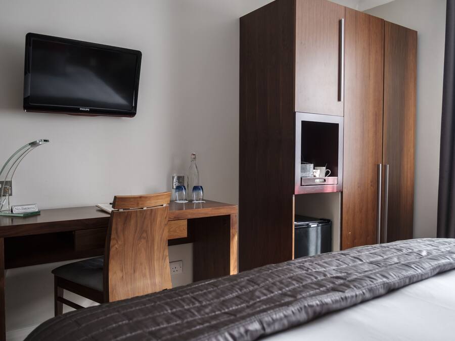 Quarto de hotel com cama, escrivaninha com cadeira, televisão fixada na parede e guarda-roupa.