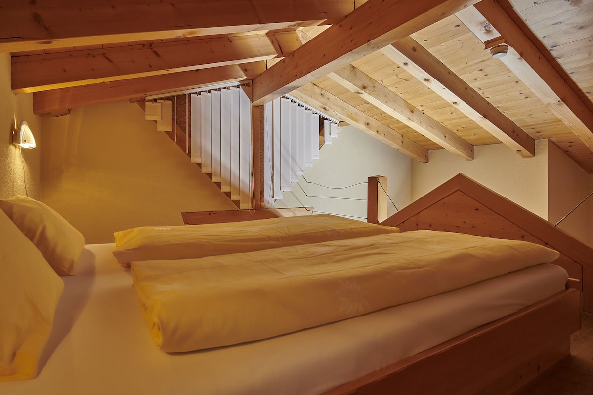Quarto com teto de madeira, escada e cama com roupa de cama amarela.