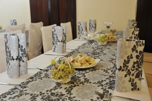 Uma mesa de jantar posta com toalhas de mesa estampadas com flores, uma cesta de vegetais verdes e um prato de doces.