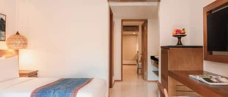 Quarto de hotel com duas camas, uma escrivaninha, uma cadeira, um abajur e uma pequena mesa com uma fruteira.