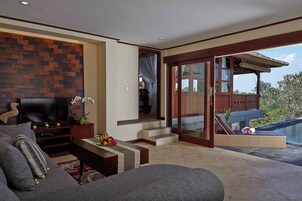 Uma sala de estar moderna com televisão de tela plana, sofá e mesa de centro. Há uma escada que leva a um balcão com vista para o exterior.