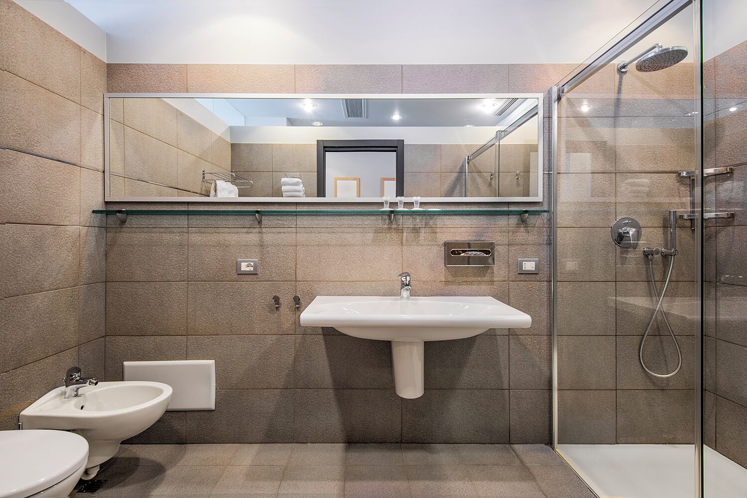 Um banheiro moderno com box de vidro, pia de pedestal e bidê.