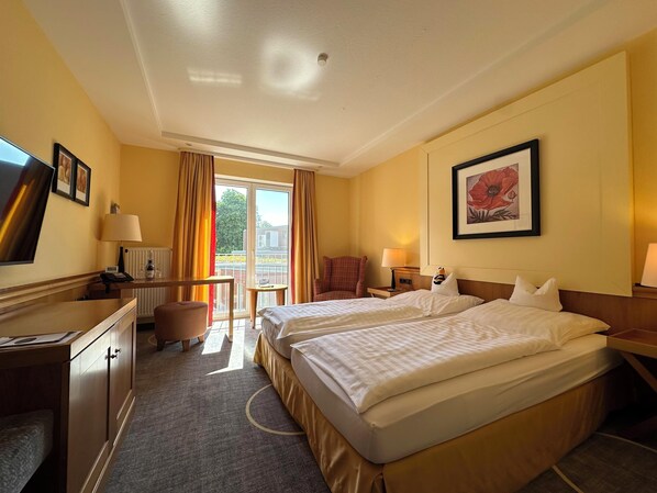 Quarto de hotel com cama, escrivaninha, cadeira, televisão e janela com cortinas.