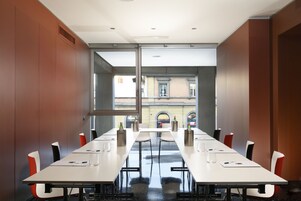 Uma sala de conferências com uma mesa comprida, cadeiras e vista para edifícios através de grandes janelas.